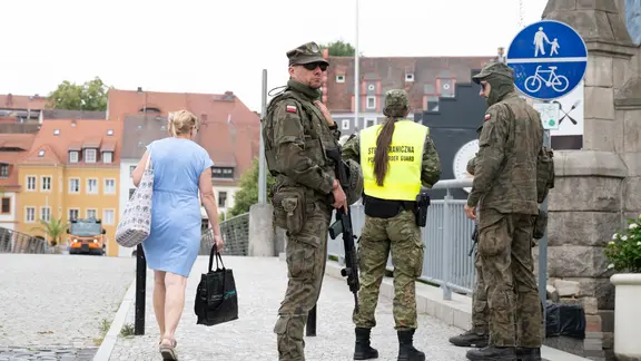 Mehrere schwer bewaffnete Grenzbeamte bewachen eine Fußgängerbrücke an der Grente.