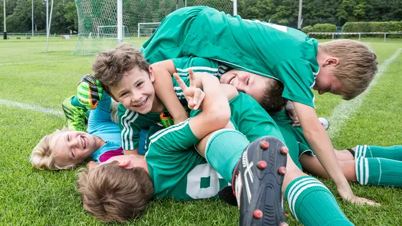 Eimn Gruppe von Kindern in grünen Trikots liegen auf dem Rasen.