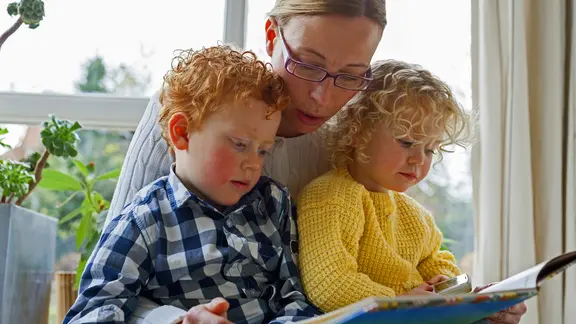 Eine Frau liest einem kleinen Jungen und einem kleinen Mädchen aus einem Buch vor.