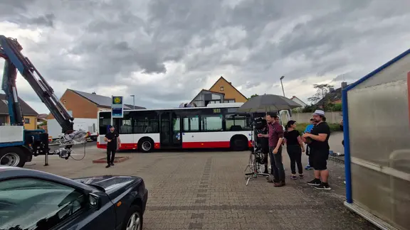 Auf einem Supermarktparkplatz stehen Personen mit Filmkameras.